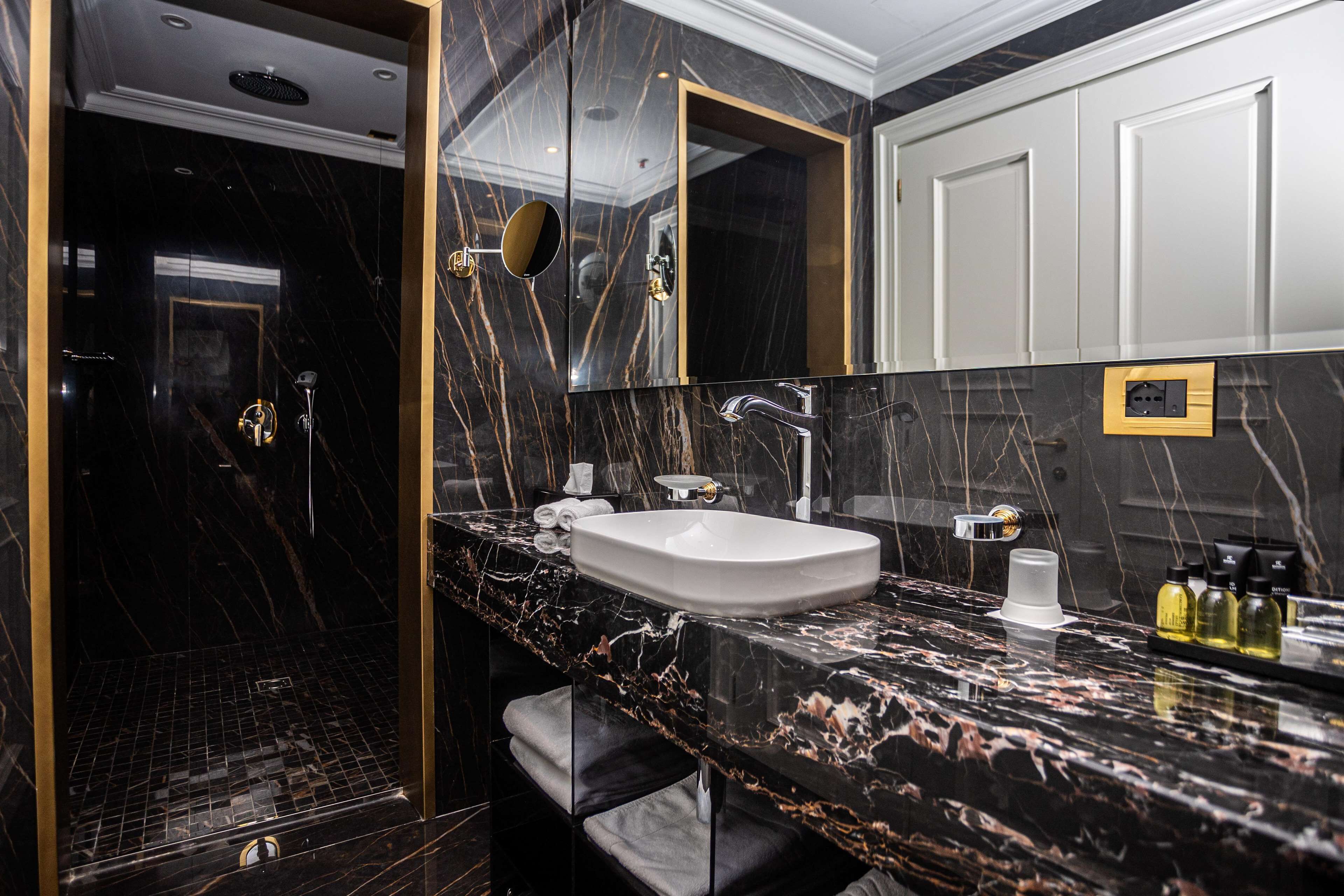 Casa de banho moderna com bancada de mármore preto, lavatório branco e espelho grande.