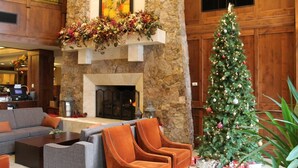 Um hall com lareira de pedra, árvore de Natal e área de estar com sofás e poltronas.