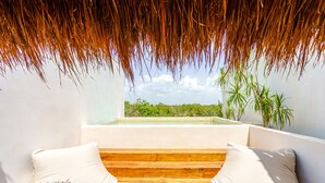 Um deck de madeira com duas almofadas brancas, um telhado de palha e vista para vegetação.