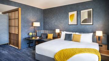 Quarto de hotel com uma cama grande, área de estar com uma mesa e um guarda-roupa.