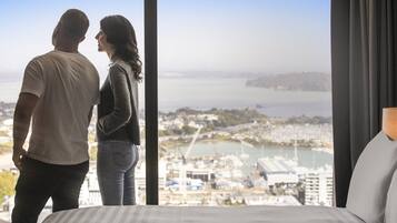 Um casal em pé perto de uma grande janela com vista para um calçadão e a paisagem urbana.