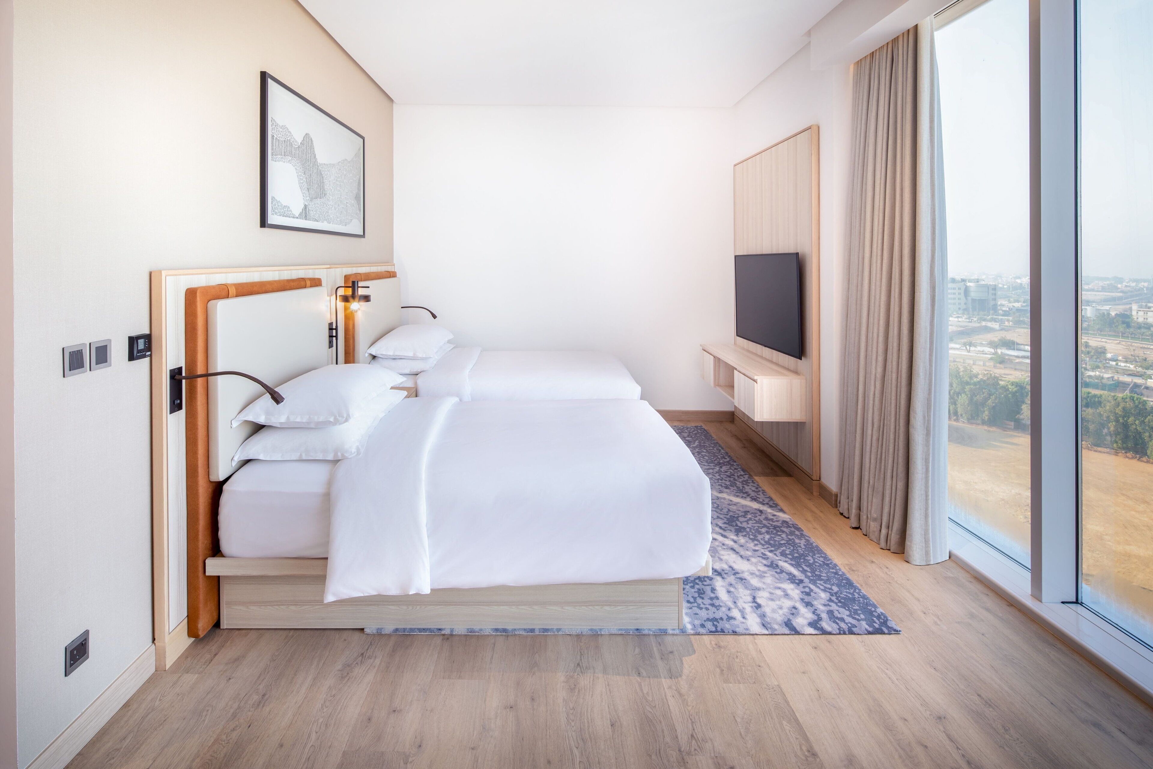 Quarto de hotel moderno com uma cama grande, televisão de tela plana e vista para a cidade.
