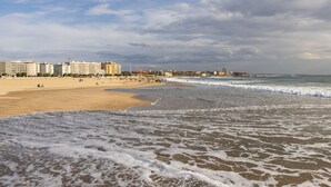 Uma praia com ondas, edifícios e um céu nublado.