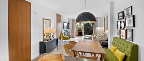 Uma sala de estar moderna com uma mesa de jantar de madeira, sofá verde e uma grande luminária pendente preta.