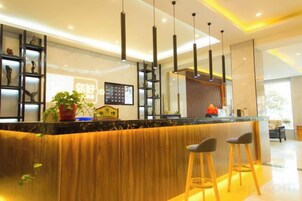 Uma área de recepção moderna com balcão de madeira, banquetas, iluminação pendente e um quadro de menu à vista.