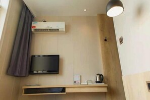 Quarto com ar condicionado fixado na parede, televisão de tela plana, prateleira de madeira com chaleira e luminária pendente.