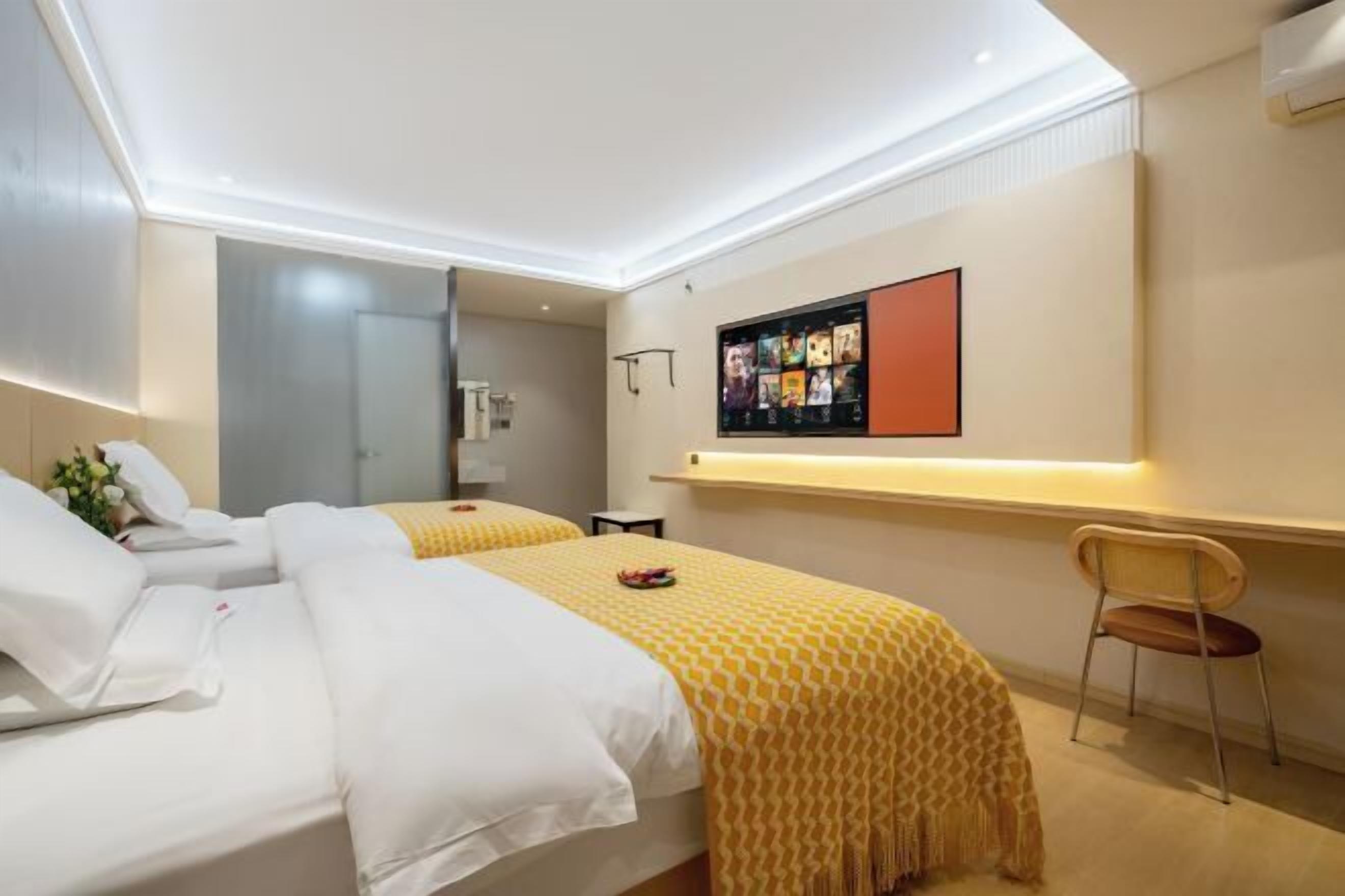 Quarto de hotel com duas camas, uma televisão presa à parede e uma pequena escrivaninha com uma cadeira.