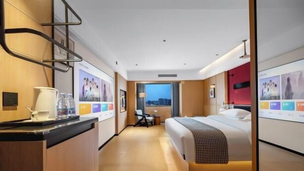 Quarto de hotel com cama, escrivaninha, cadeira, mesa pequena e janela vista para a cidade.