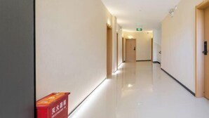Corredor de hotel limpo e moderno, com piso polido, portas de madeira e extintor de incêndio à esquerda.