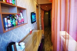 Quarto de hotel com um banco de madeira, televisão na parede e prateleiras com diversos artigos de higiene pessoal.