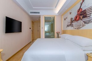 Quarto de hotel com uma cama grande, televisão de tela plana na parede e um mural com instrumentos musicais e livros.