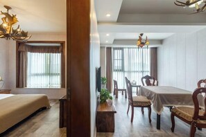 Quarto de hotel com cama, mesa de jantar com cadeiras, um banco de madeira e um candelabro.