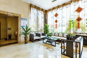 Um saguão de hotel com balcão de recepção, área de estar e grandes janelas com cortinas.