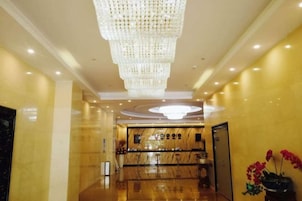Um saguão de hotel com um grande candelabro, um balcão de recepção e piso lustroso.