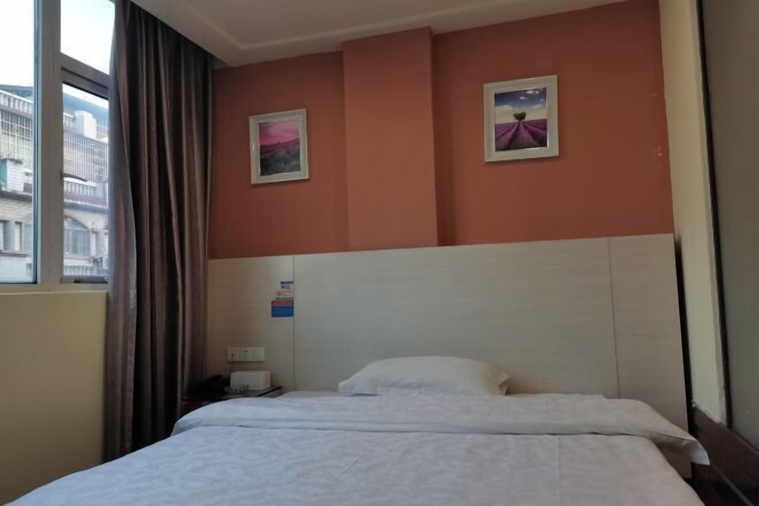 Quarto de hotel com cama, mesa de cabeceira, janela com cortinas e duas imagens emolduradas na parede.
