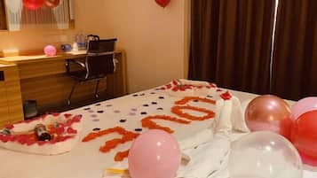 Quarto de hotel com uma cama coberta de pétalas de rosa e balões formando a palavra 'LOVE'.