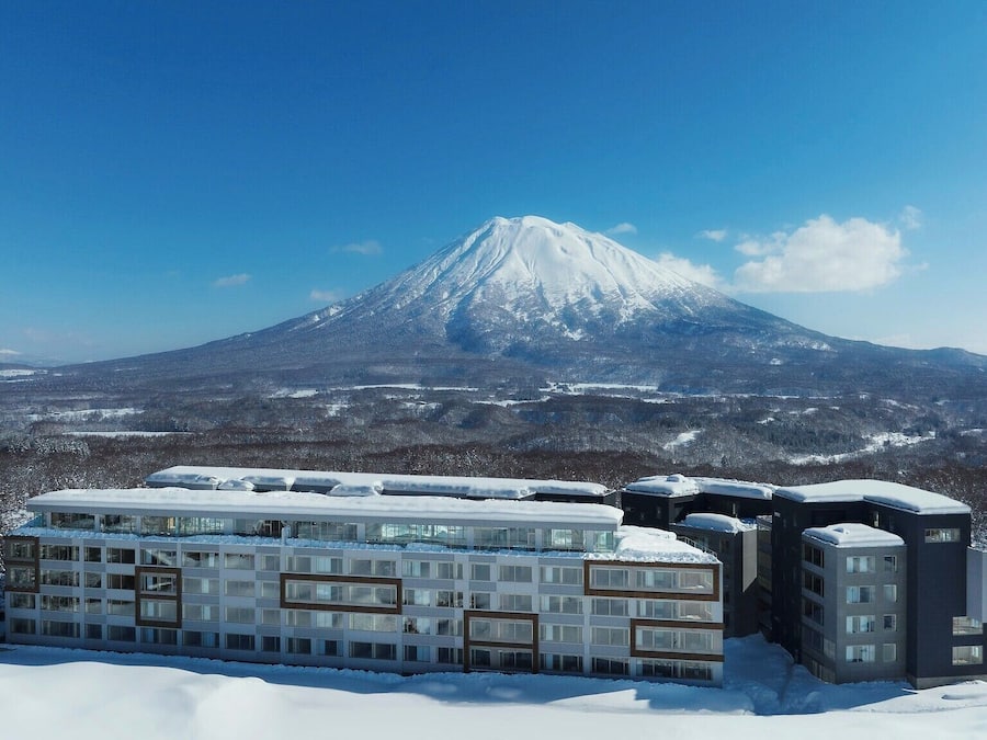 Um hotel moderno com vários andares, grandes janelas e vista para uma montanha coberta de neve.