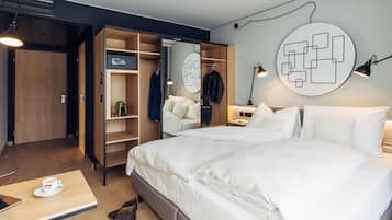 Quarto de hotel moderno com uma cama grande, uma escrivaninha com um laptop e uma chávena, um guarda-roupa e um espelho.