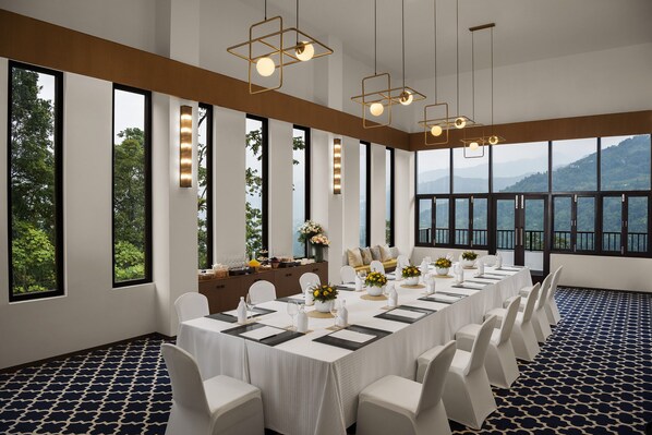 Uma sala de conferências com uma mesa comprida preparada para uma reunião, grandes janelas com vista para as montanhas e iluminação pendente moderna.