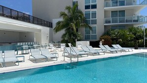 Piscina com espreguiçadeiras e uma palmeira, cercada por um edifício moderno com várias varandas.