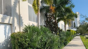 Um edifício moderno com varandas, calçada bem cuidada e vegetação exuberante.