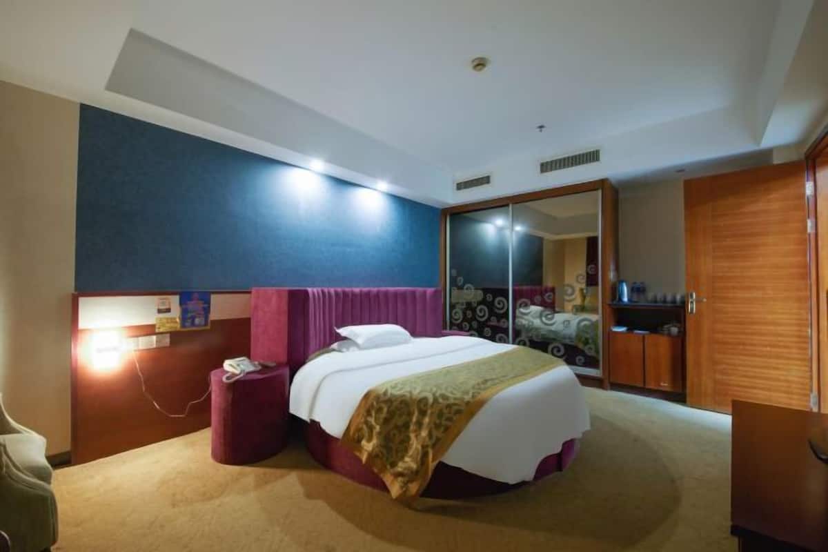 Quarto de hotel com uma cama, uma escrivaninha, uma cadeira, um guarda-roupa e um espelho.