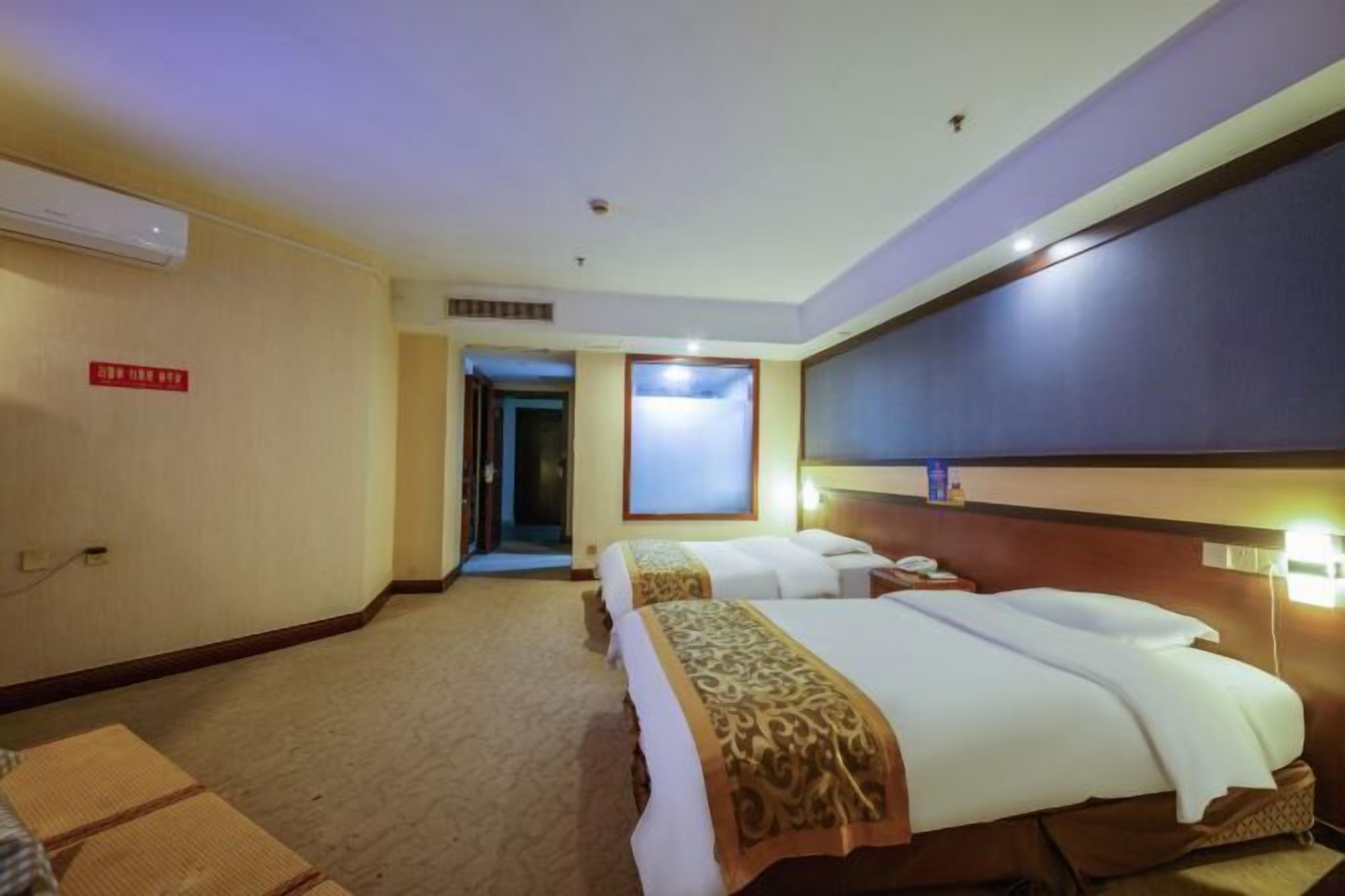Quarto de hotel com duas camas, um espelho grande e uma porta que dá para um corredor.