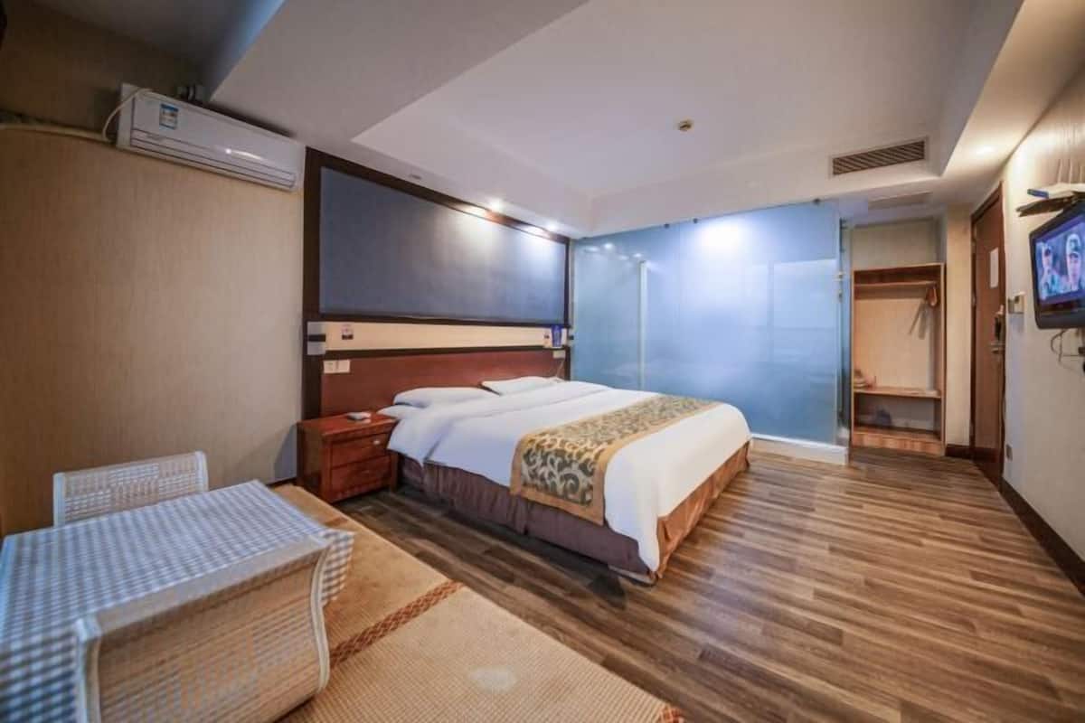 Quarto de hotel com uma cama grande, uma mesinha de cabeceira, uma televisão e um guarda-roupa.