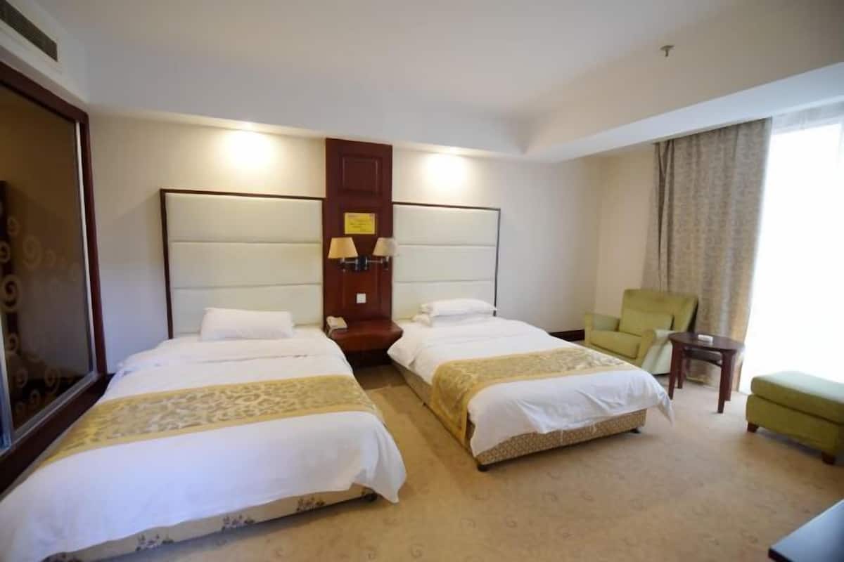 Quarto de hotel com duas camas, uma escrivaninha, uma cadeira e um sofá.