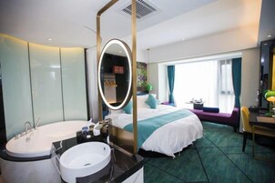 Quarto de hotel com cama grande, banheiro separado com banheira, escrivaninha e janela com cortinas.