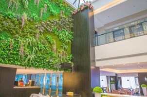 Um saguão de hotel com jardim vertical, área de estar e balcão de recepção.