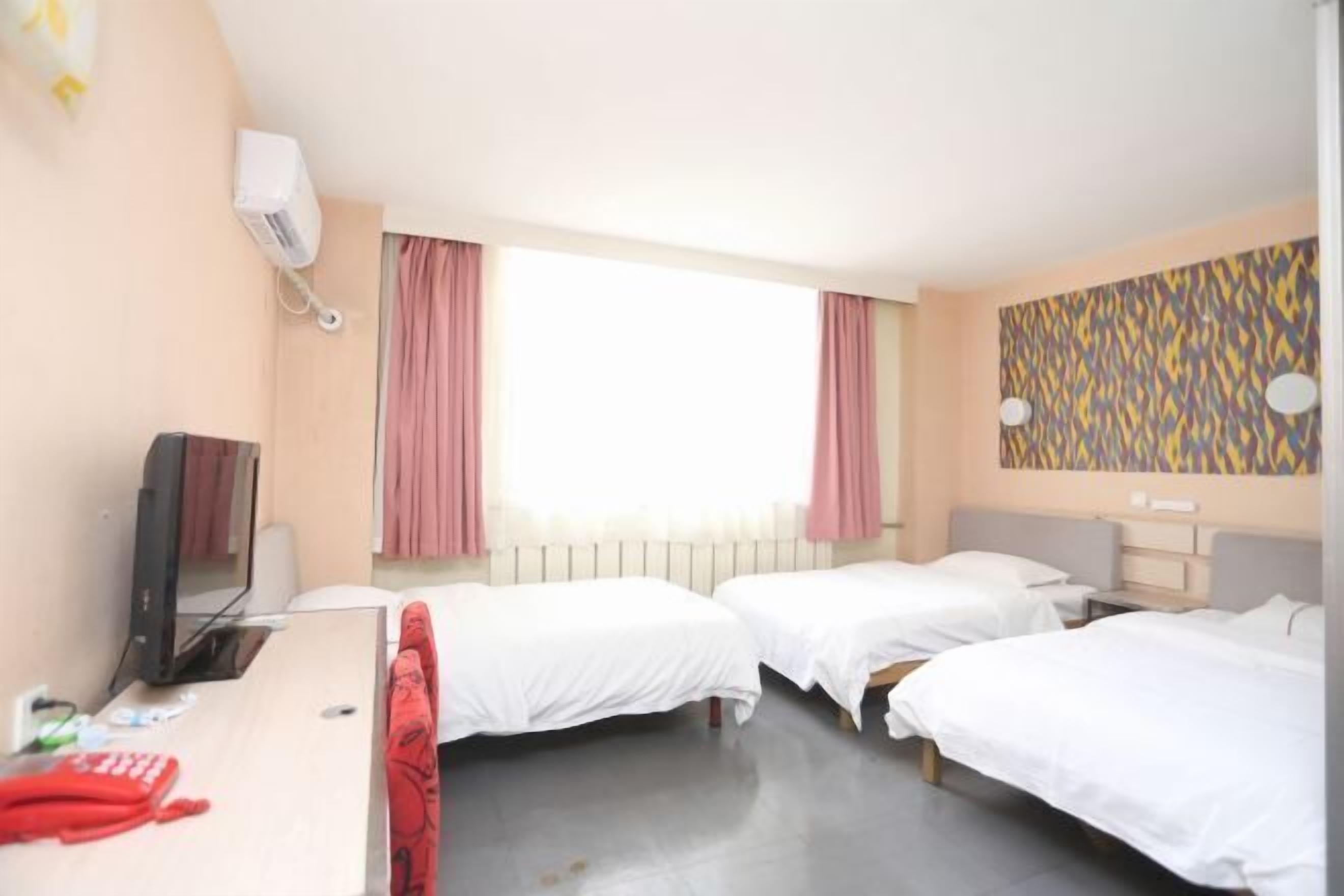 Quarto de hotel com duas camas, uma escrivaninha com computador, televisão e parede com padrão.