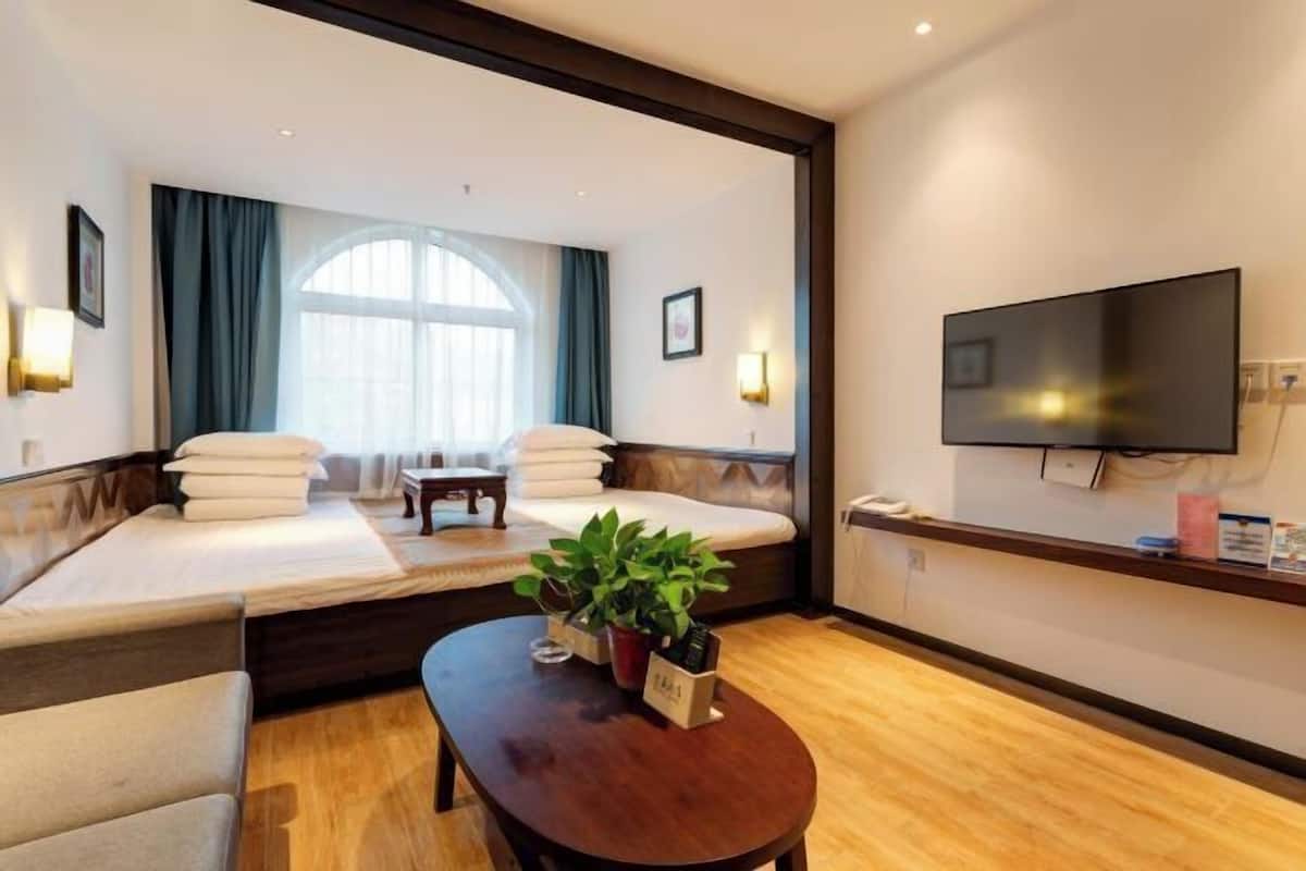Quarto de hotel com duas camas, uma televisão, uma pequena mesa com uma planta e uma janela com cortinas.
