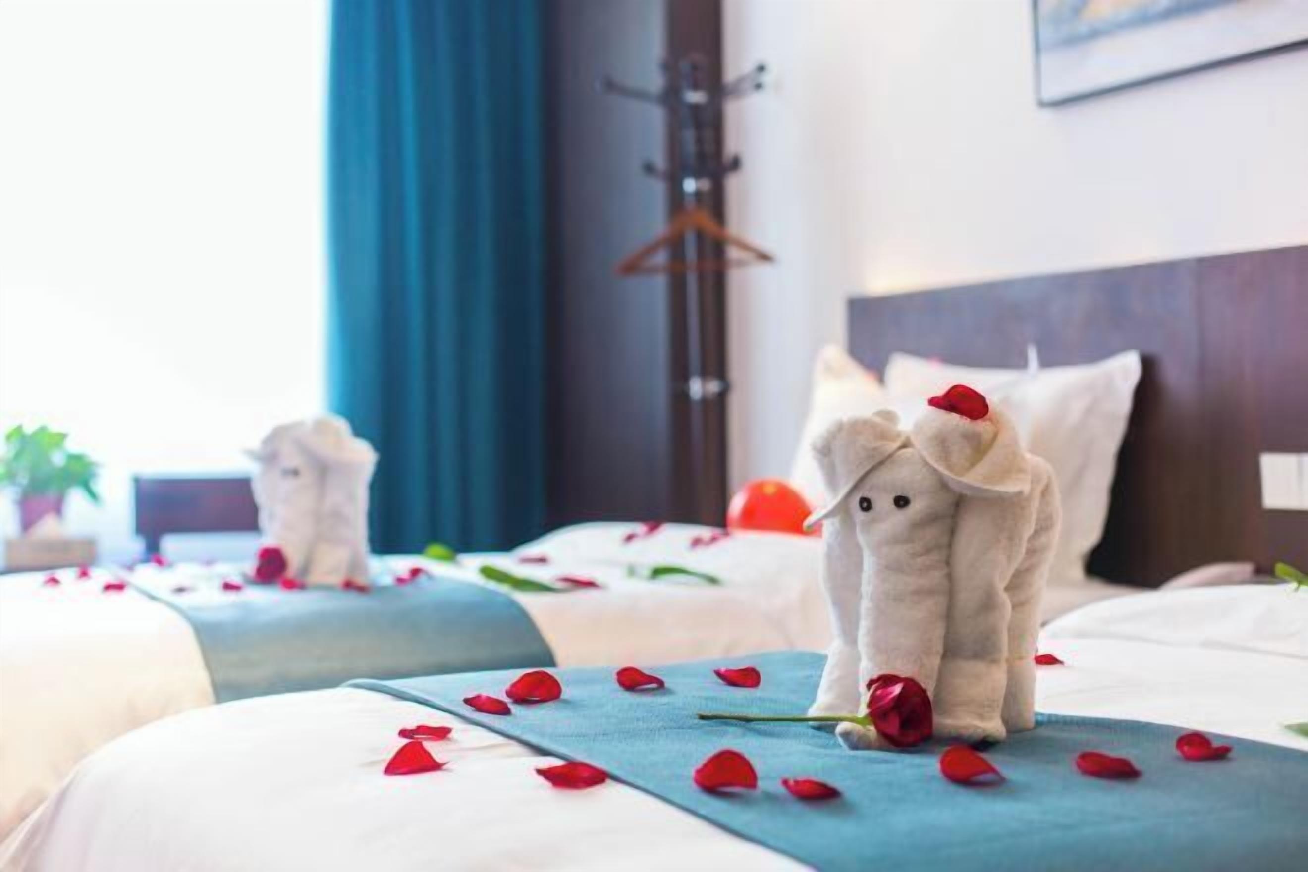 Quarto de hotel com duas camas, cada uma decorada com pétalas de rosa e um ursinho de pelúcia.