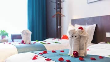 Quarto de hotel com duas camas, cada uma decorada com pétalas de rosa e um ursinho de pelúcia.