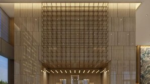 Um lobby com design moderno, com um balcão de recepção de mármore, uma grande pintura abstrata e uma estrutura de teto em formato de grade.