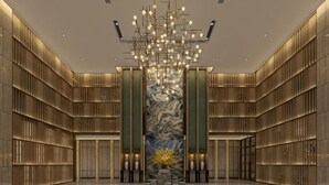 Um hall amplo com um lustre central, estantes verticais e uma parede de mármore.