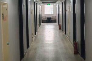 Um corredor comprido e estreito com portas em ambos os lados, extintores de incêndio e um alarme de incêndio na parede direita.