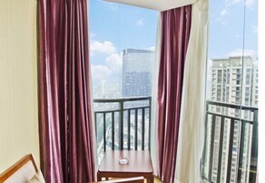 Uma varanda com vista para edifícios da cidade, uma mesa pequena e cortinas.