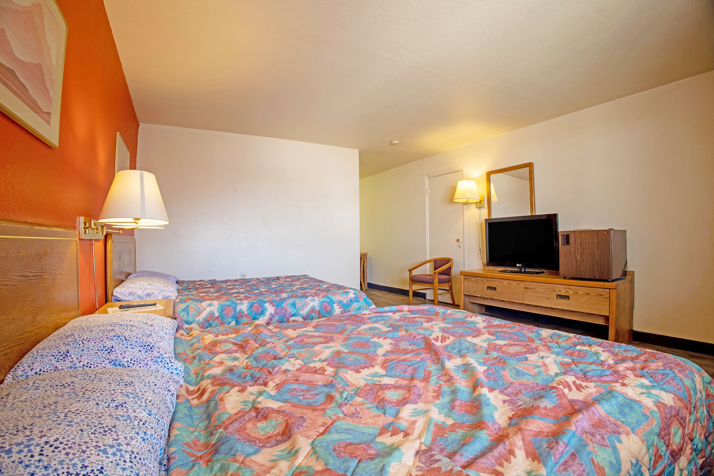 Quarto de hotel com duas camas, televisão, cómoda de madeira e uma cadeira.