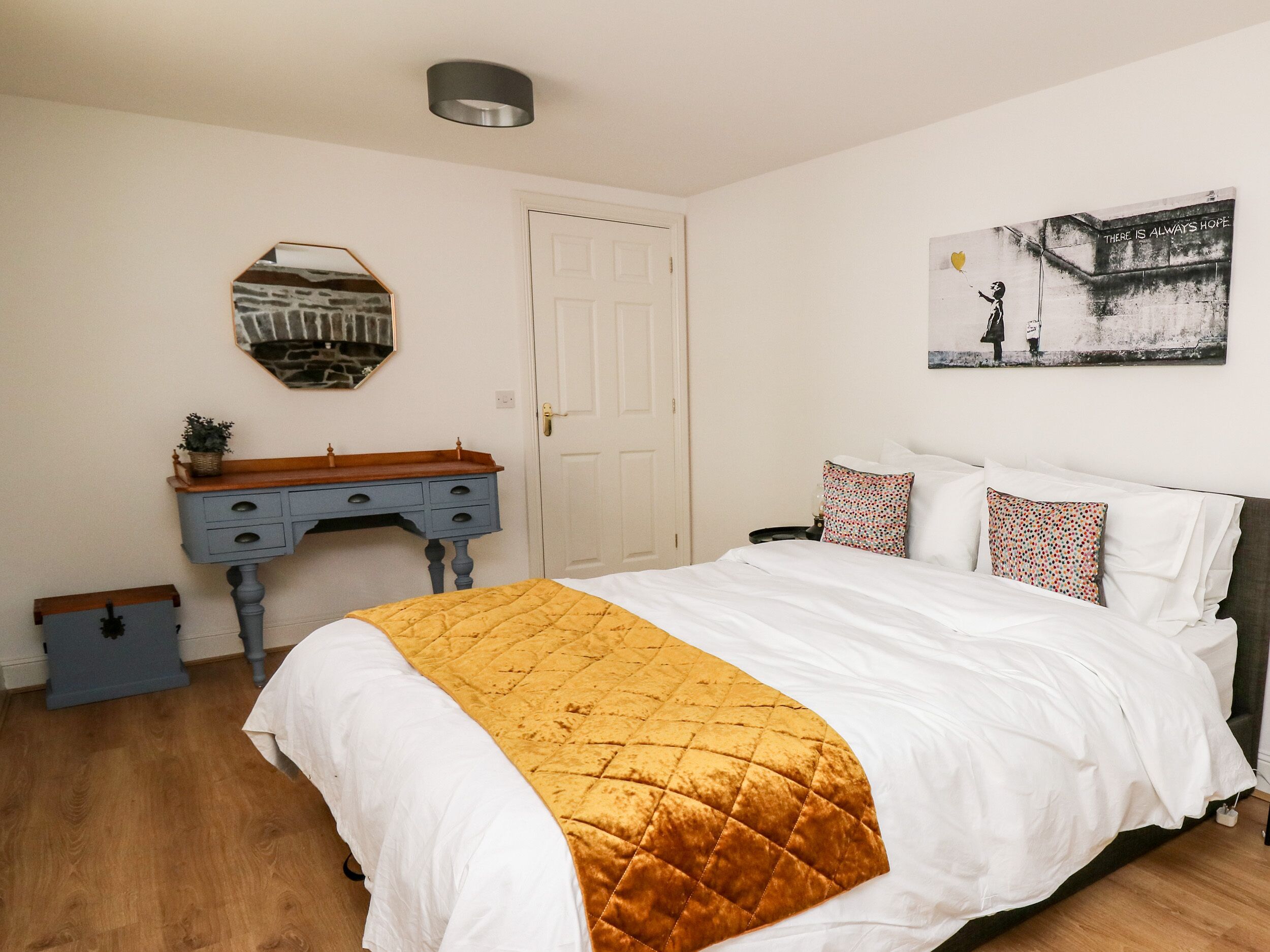 Quarto com cama, cômoda, porta e uma obra de arte na parede.