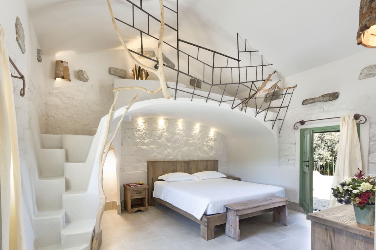 Quarto com cama de madeira, paredes brancas, escada de madeira e um design de teto único.