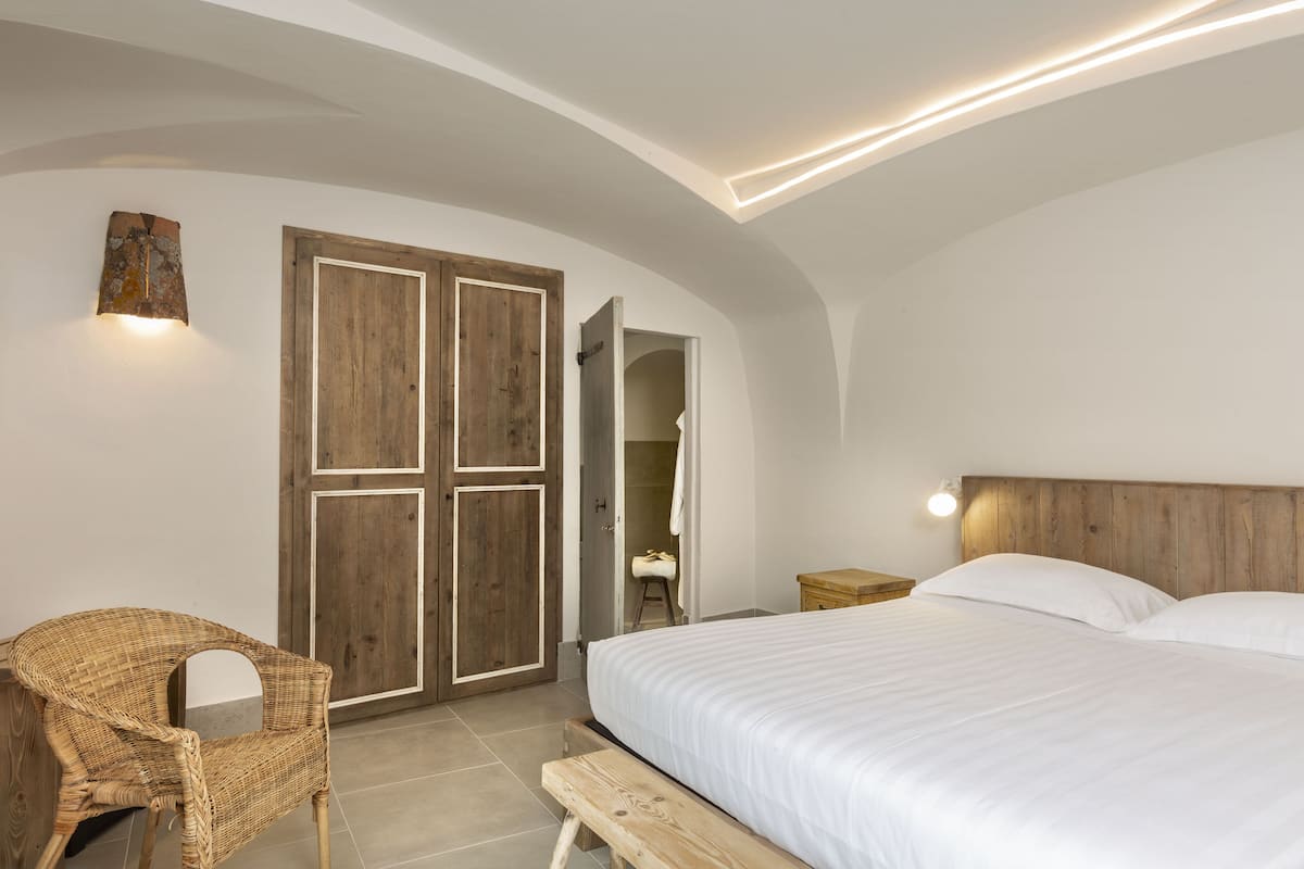 Quarto com uma cama grande, um guarda-roupa de madeira, uma cadeira de vime e um banco.