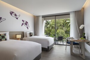 Quarto de hotel com duas camas, uma mesa de jantar e vista para o verde lá fora.