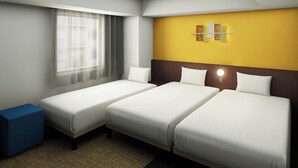 Quarto de hotel com duas camas de solteiro, um banquinho pequeno azul, uma janela grande com cortinas translúcidas e uma parede amarela com obras de arte.