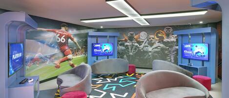 Uma sala de jogos moderna com várias telas, assentos confortáveis e um mural vibrante na parede.