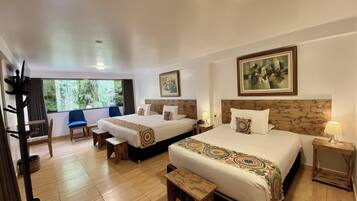 Quarto de hotel com duas camas, uma janela grande, uma cadeira, um banco e um porta-casacos.