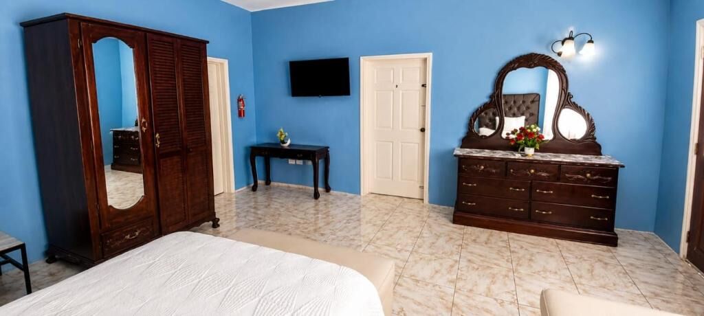 Quarto com cama, guarda-roupa, penteadeira, televisão e porta.