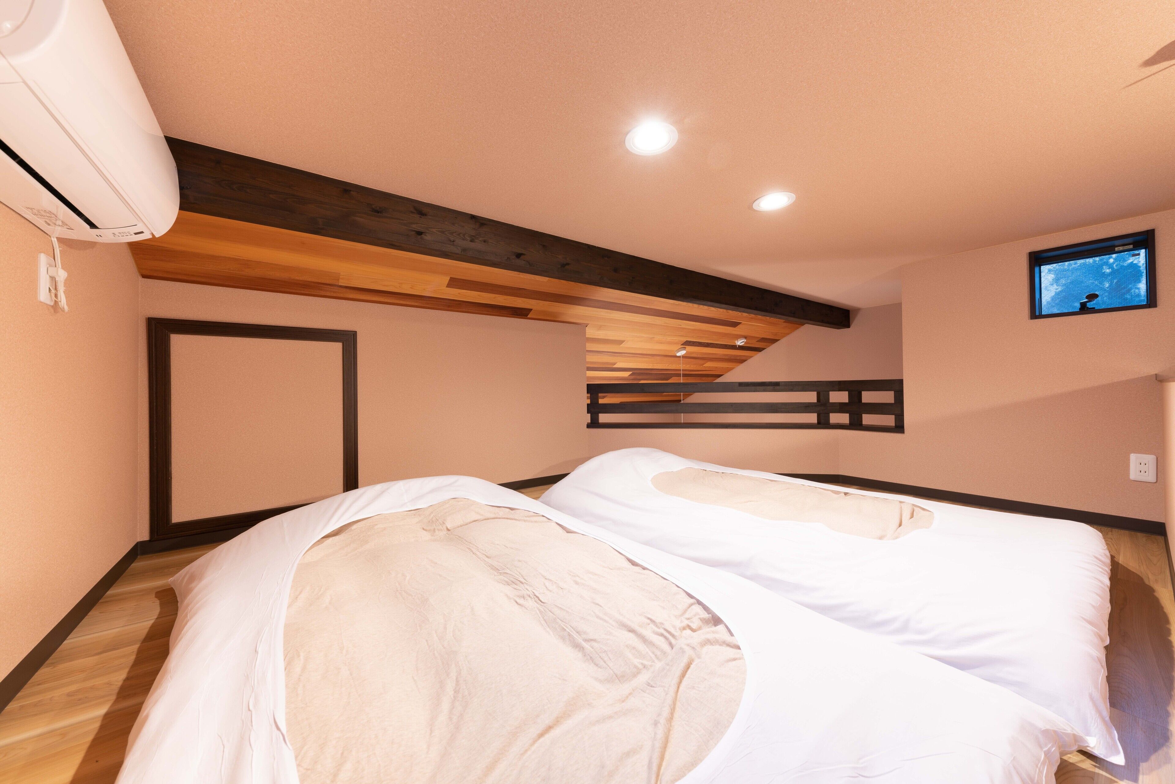 Quarto com duas camas, vigas de madeira no teto, uma janela pequena e um aparelho de ar condicionado.