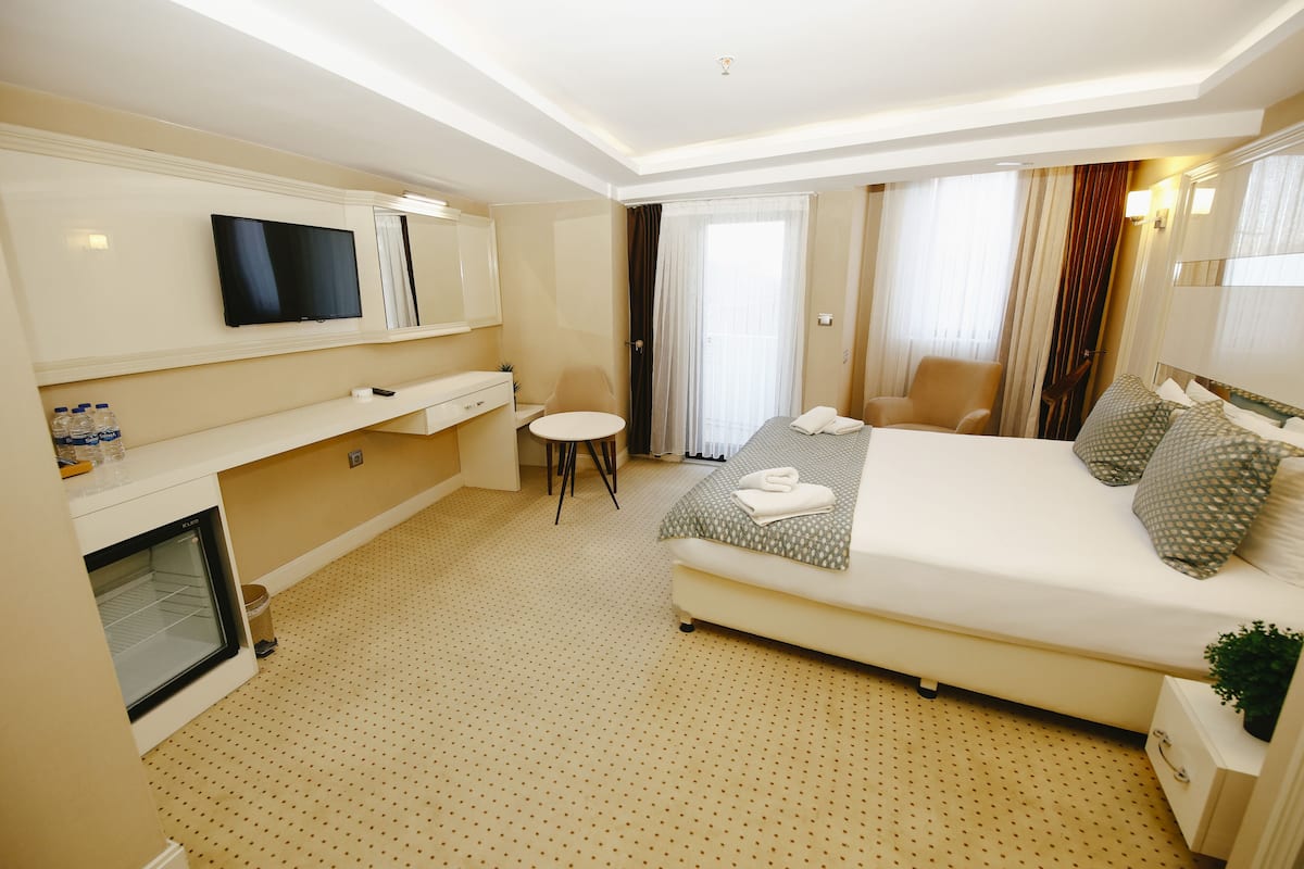 Quarto de hotel com cama, televisão, escrivaninha, cadeira e mesa pequena.